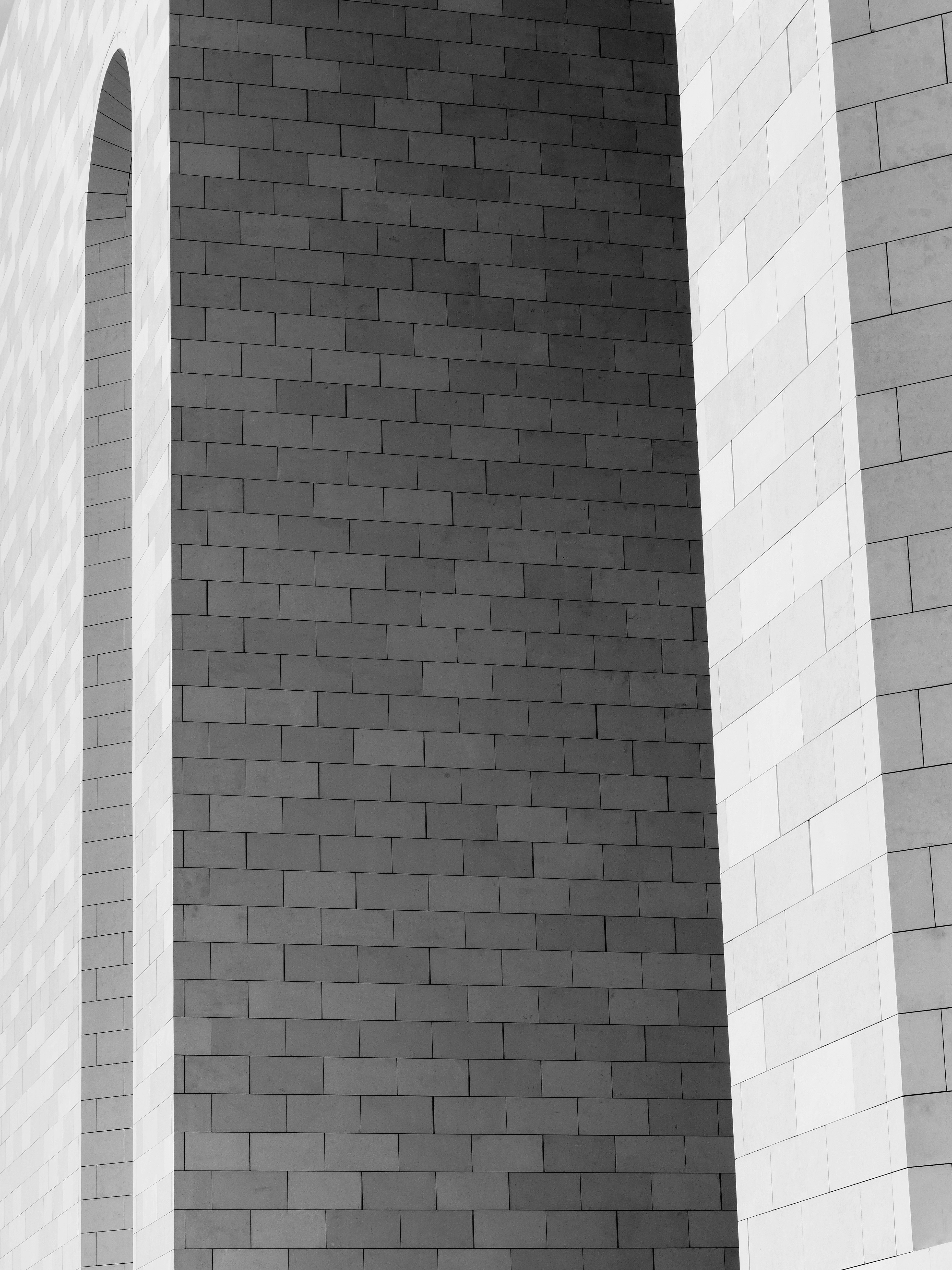 Monochrome architectural facade with intersecting planes and curved arch hints, emphasizing texture and geometry.