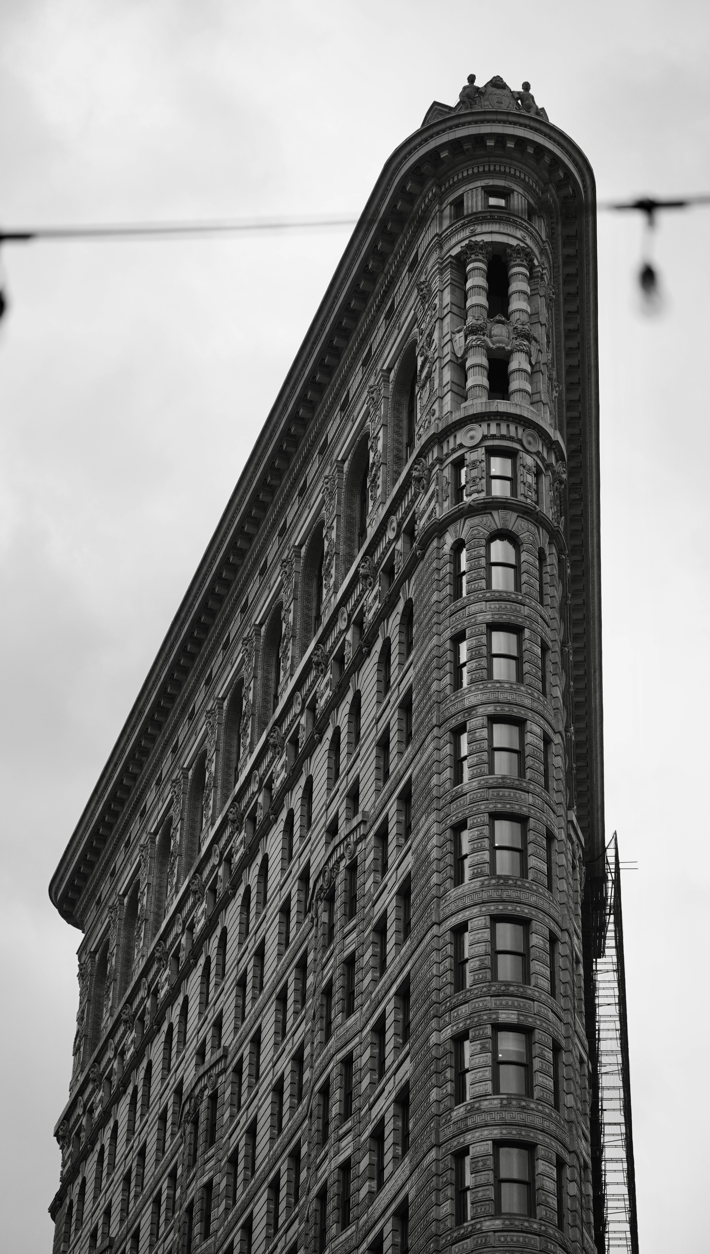 Monochrome shot of a tall, ornate urban building with curved corner, rising diagonally across the frame against a pale sky.