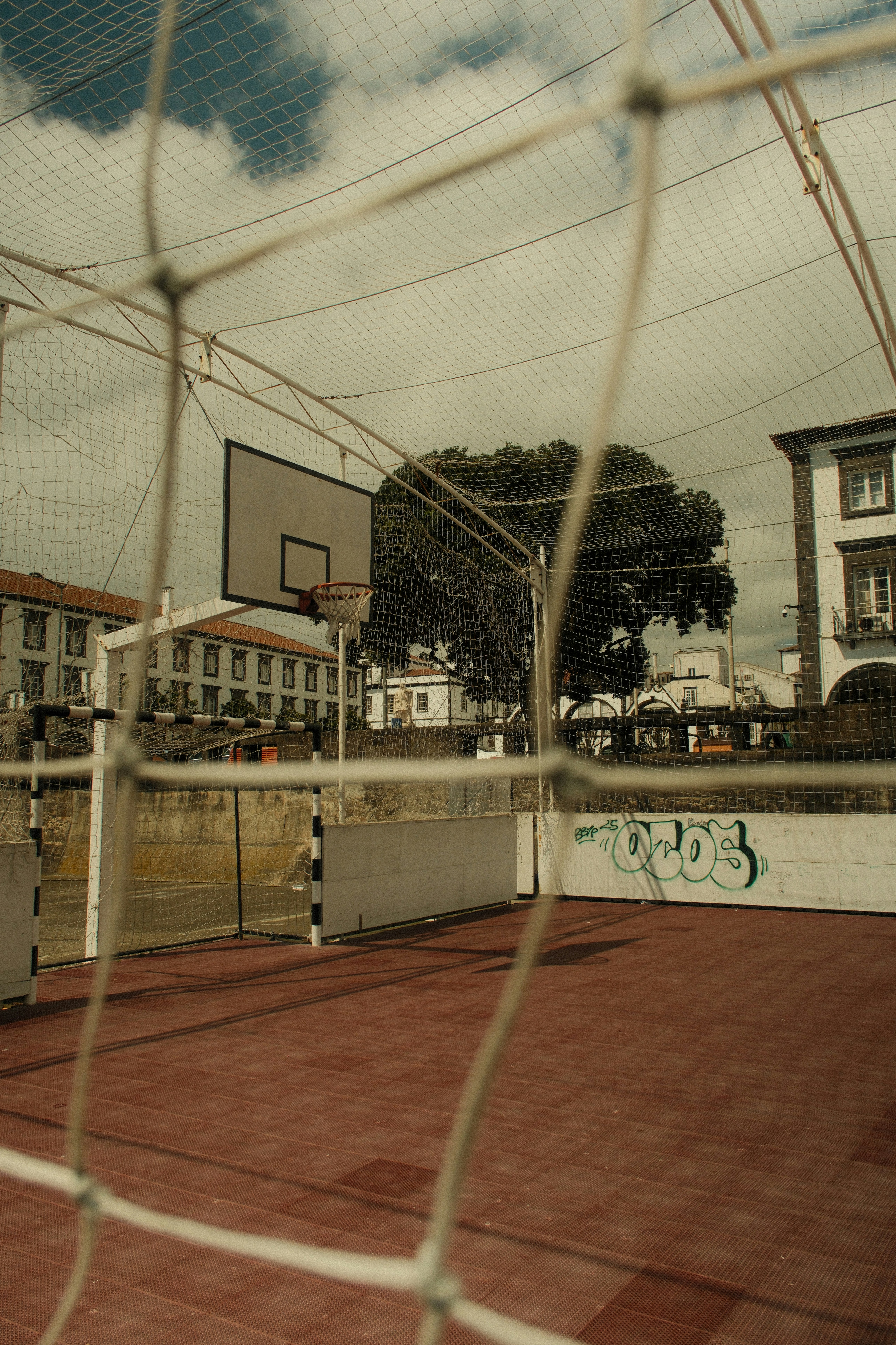 Netted Court: A Basketball Rim Framed by Faded Urban Echoes