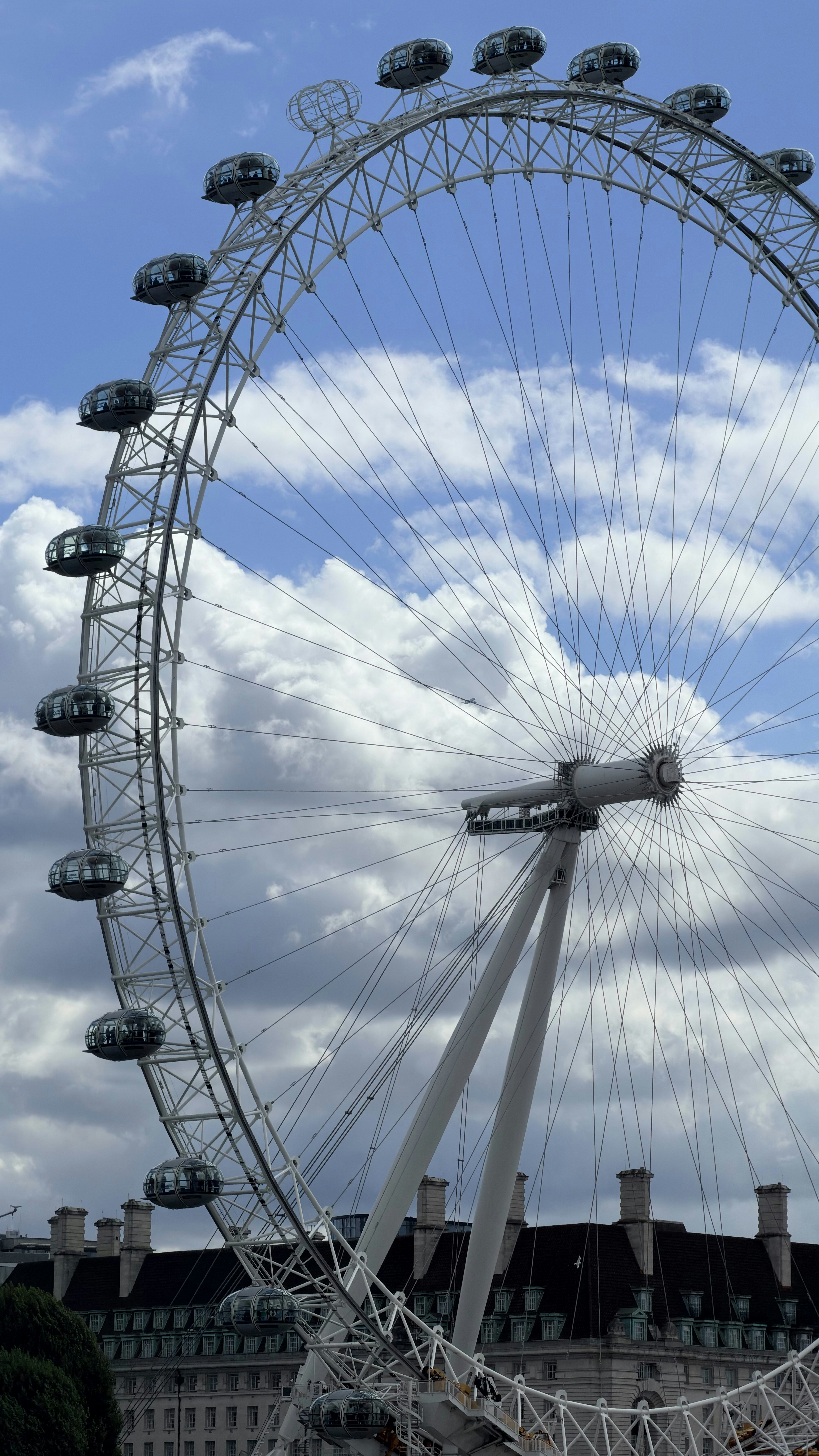 Rising Ferris wheel dominates the skyline against a blue sky with clouds; city buildings peek below, the frame emphasizing wheel spokes and capsules.