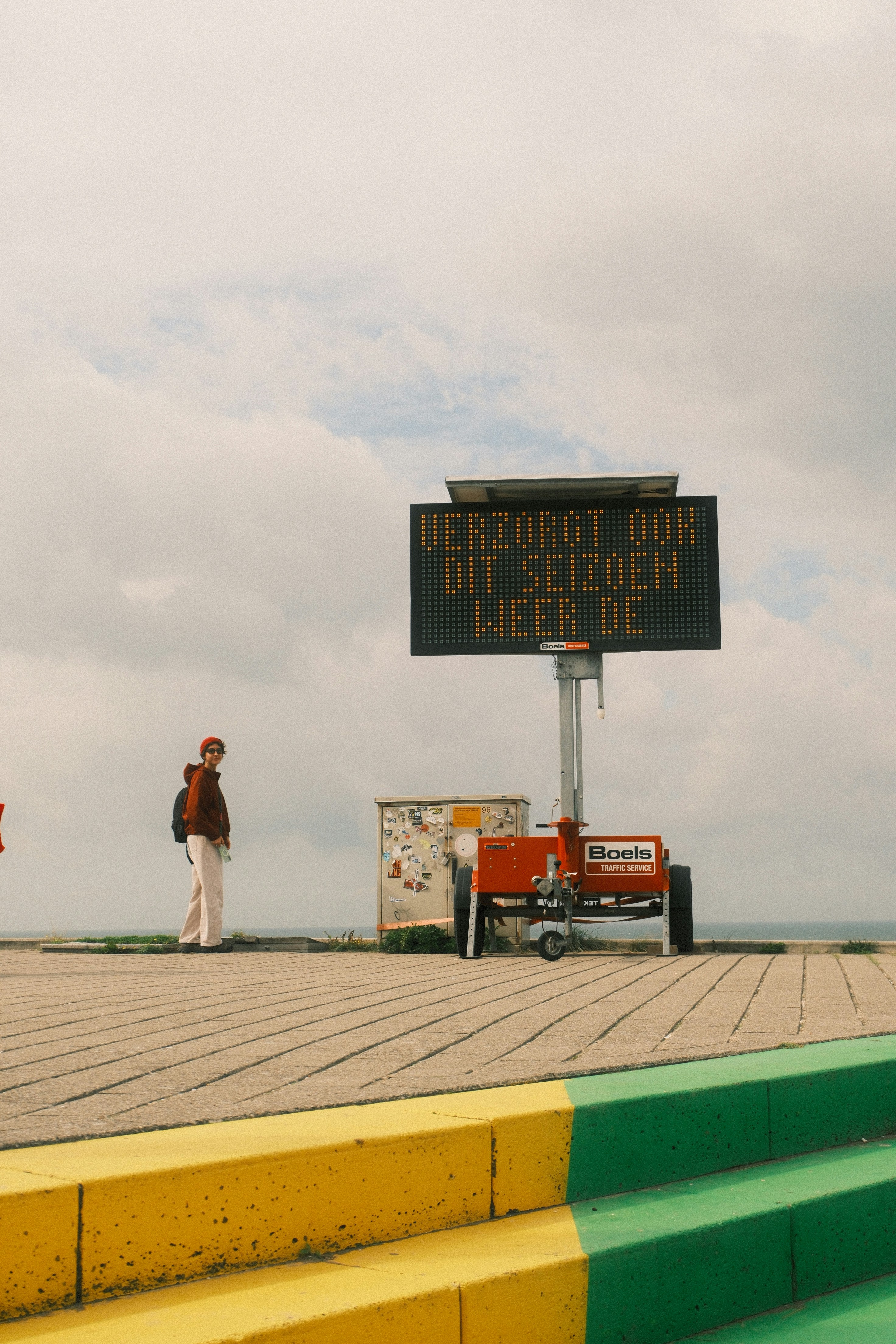 Lone Traveler by the Electronic Billboard Along a Seaside Promenade
