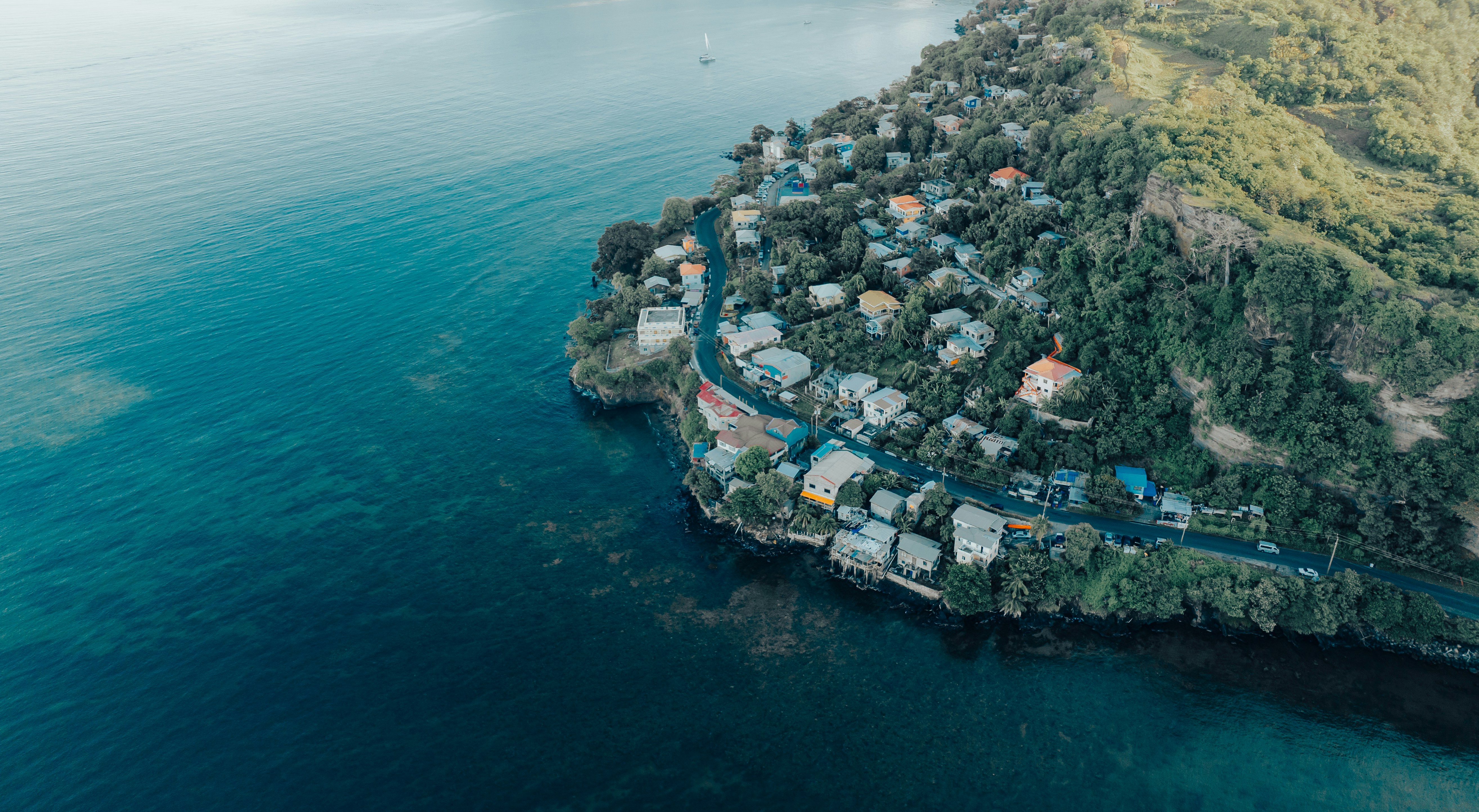 An aerial view of a coastal village nestled between a lush green hillside and the blue sea