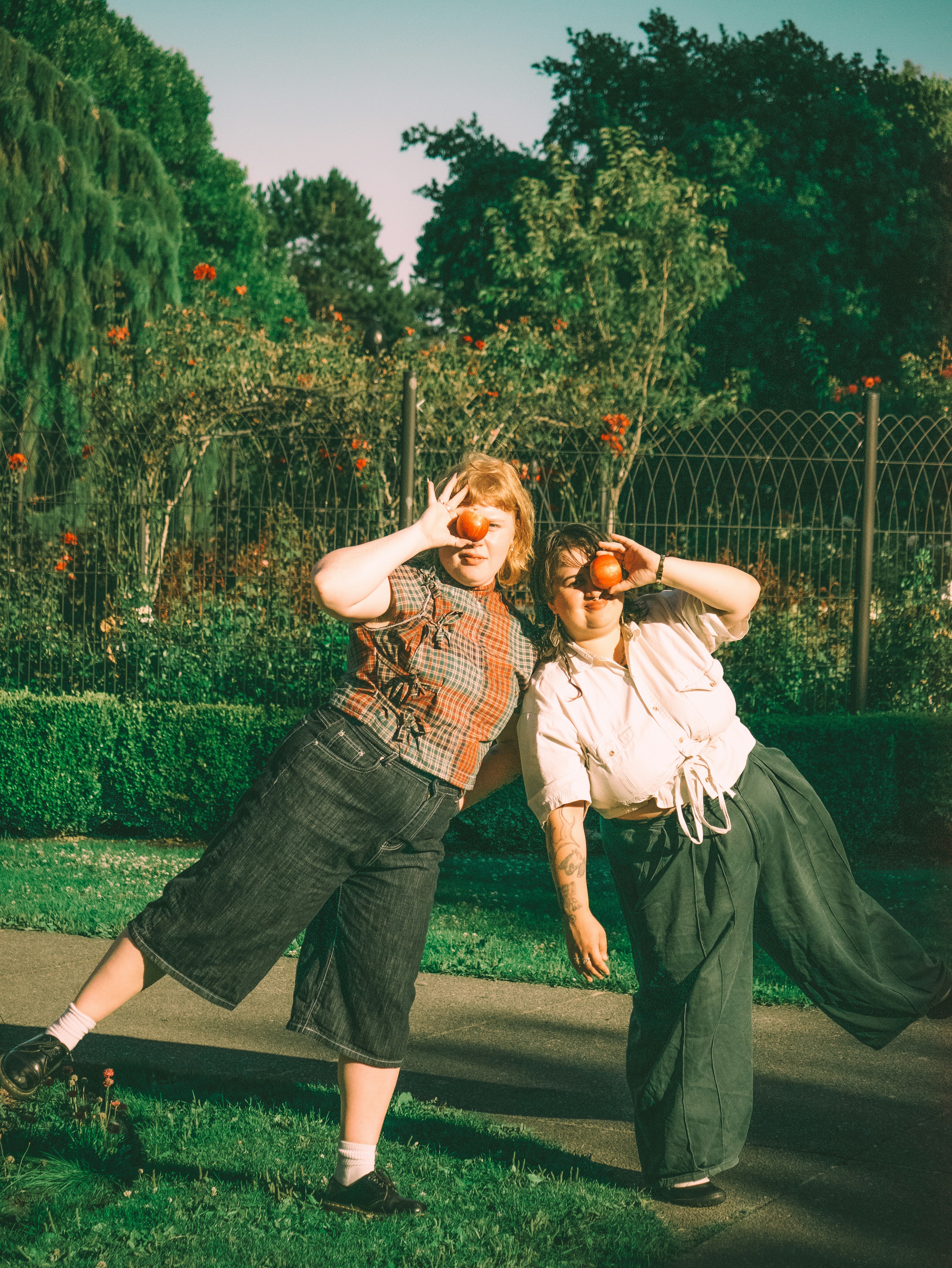 Two friends strike a playful pose under a sunlit garden arch