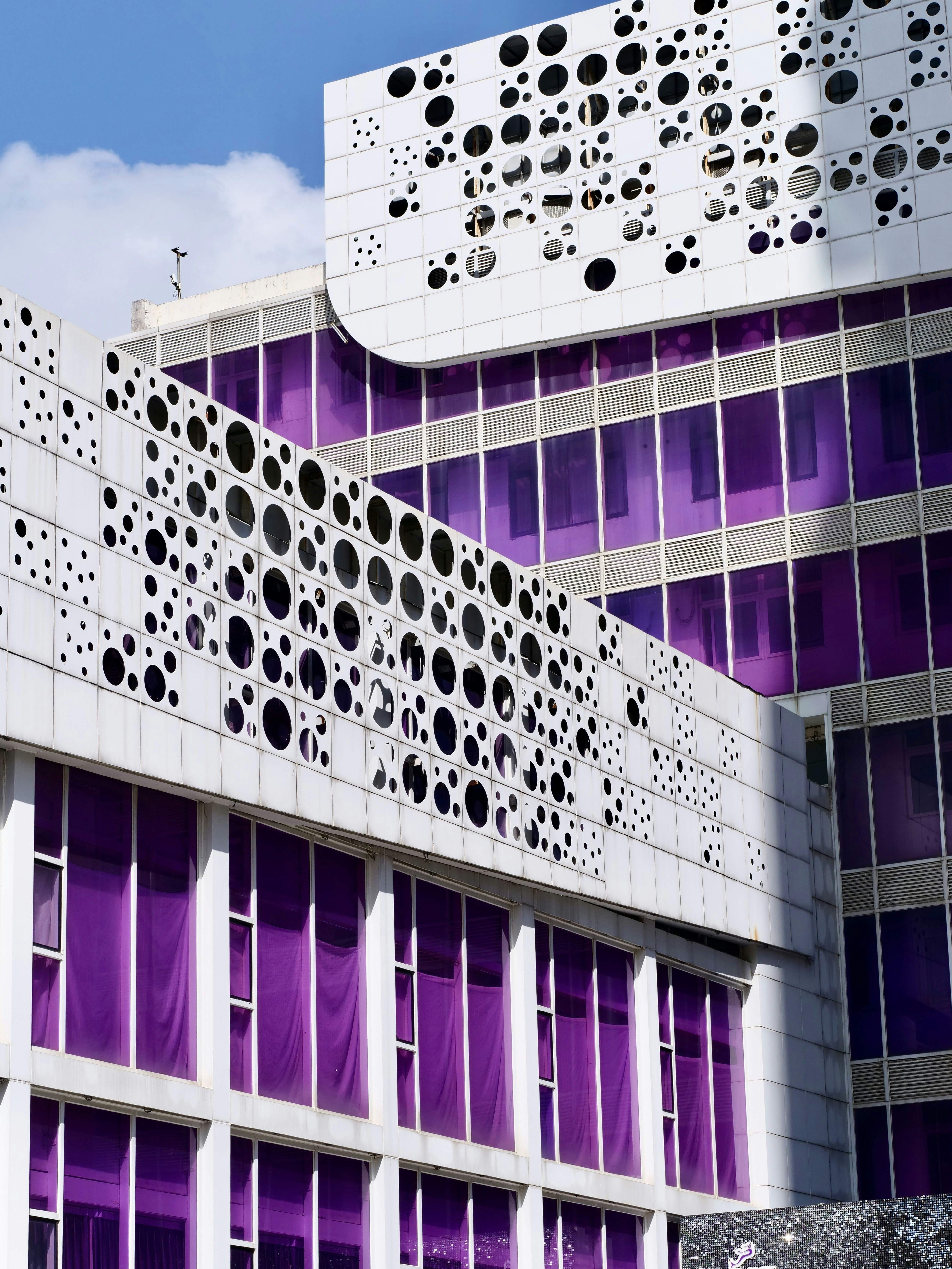Contemporary building facade with bold purple-tinted windows and a perforated white metal screen featuring circular cutouts.