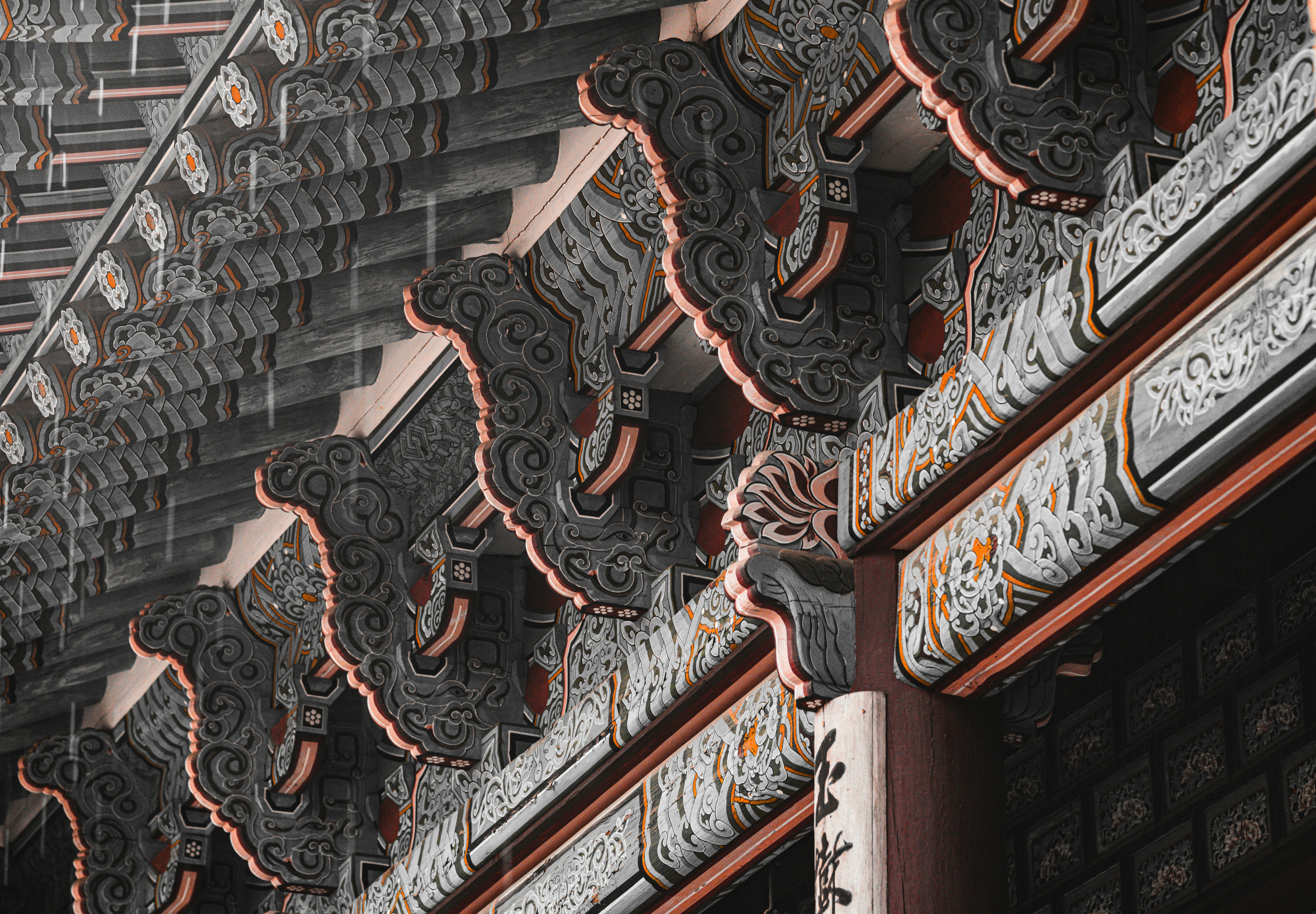 Intricate carved beams and painted brackets along a traditional Chinese eave, highlighting detailed patterns and color. The image emphasizes architectural craft and texture.