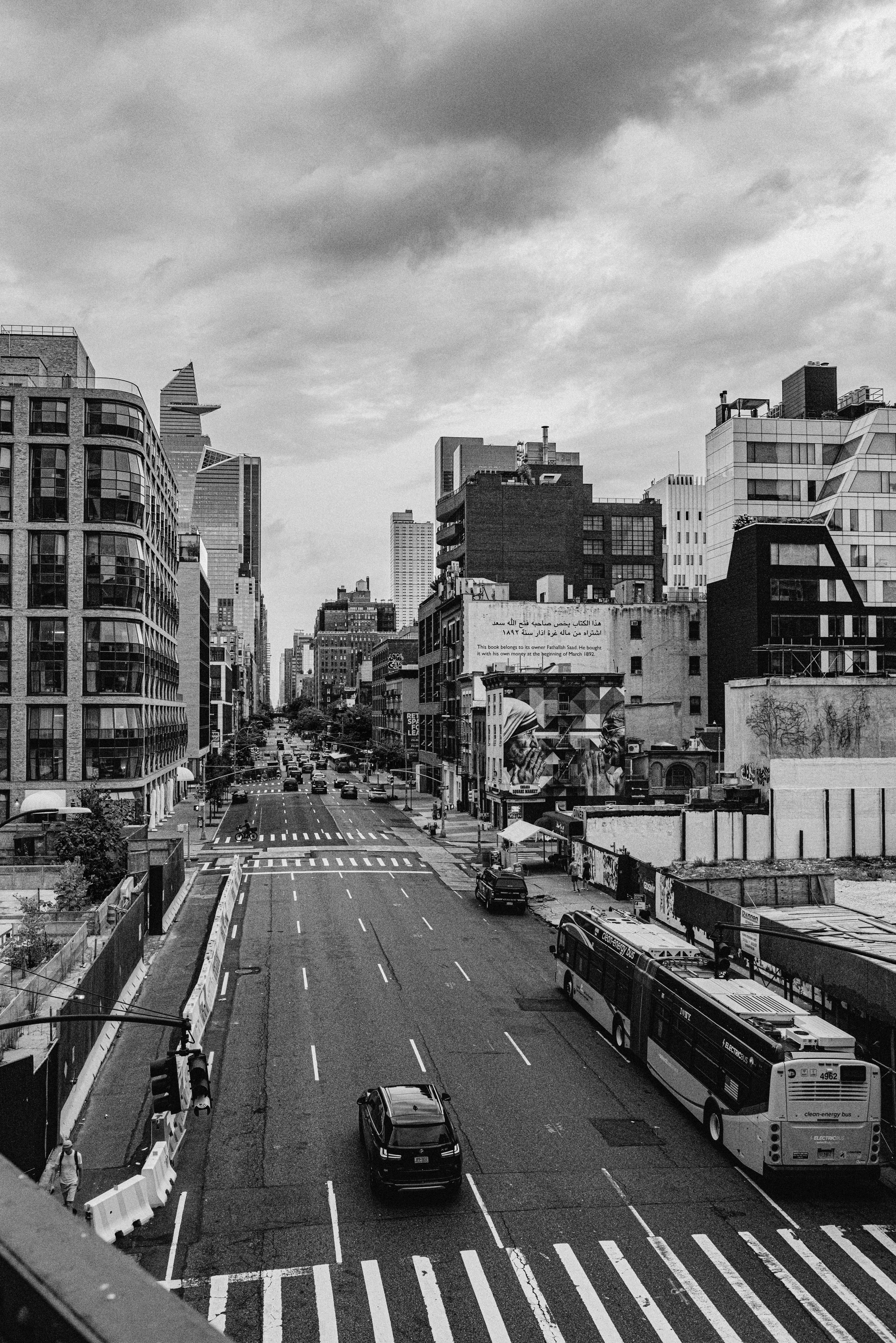 Monochrome street scene with distant cityscape, vehicles and pedestrians along a broad avenue; architectural variety and depth from foreground to horizon. This is a photographic capture, not a painting or illustration.