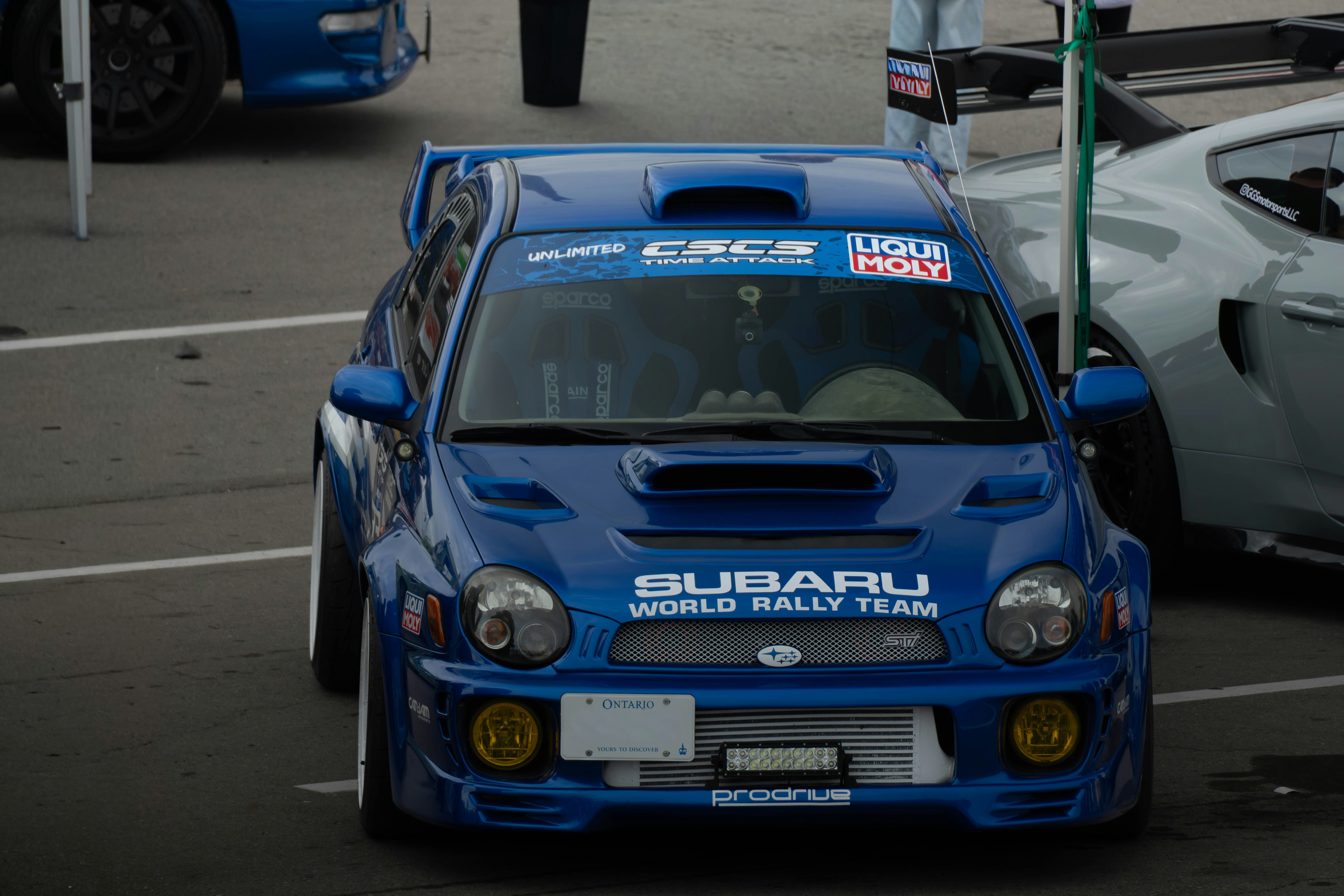 Blue Subaru rally car with prominent front fascia and sponsor decals in a paddock; emphasis on vehicle styling and race-ready details.