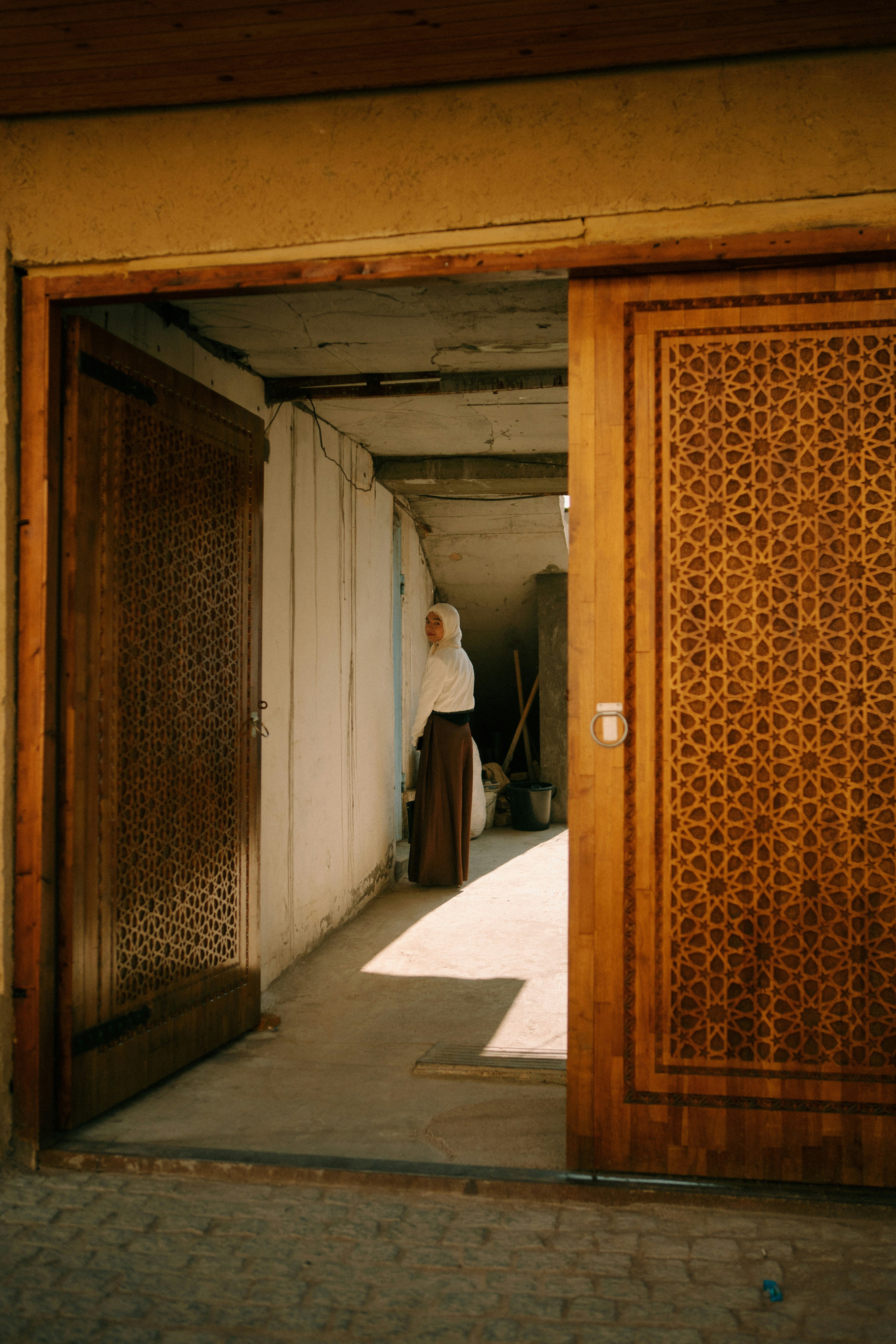 Doorway to Quiet Resolve: A Woman in Traditional Attire in Shadowed Corridor
