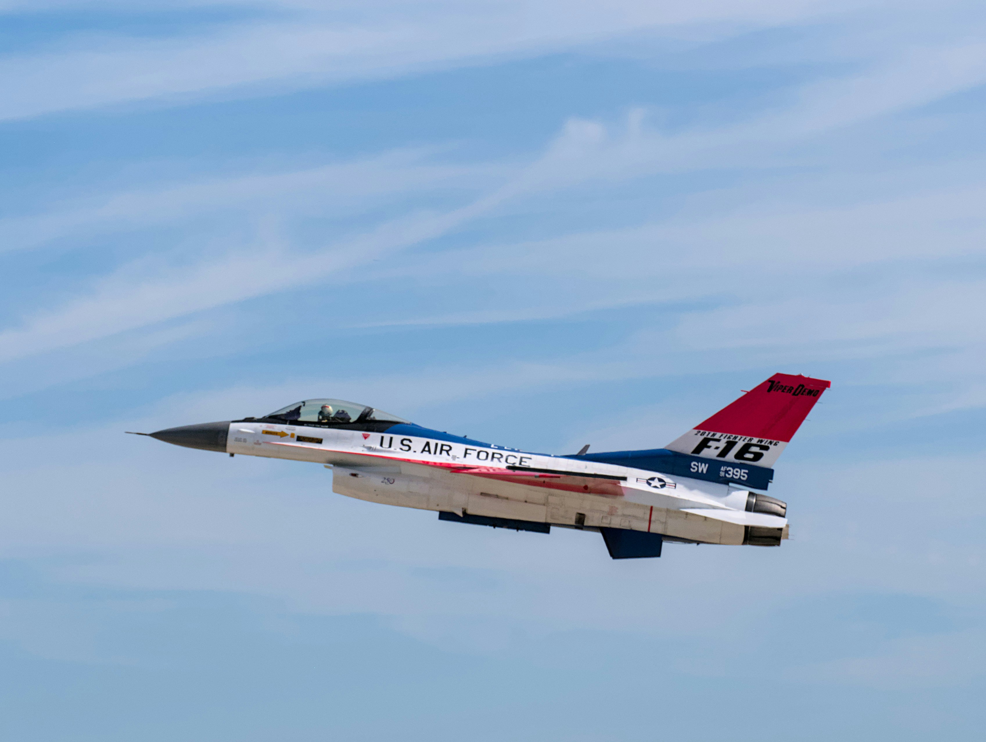 A U.S. Air Force F-16 fighter jet flies past in a clear blue sky, showcasing its streamlined profile and red tail fins.