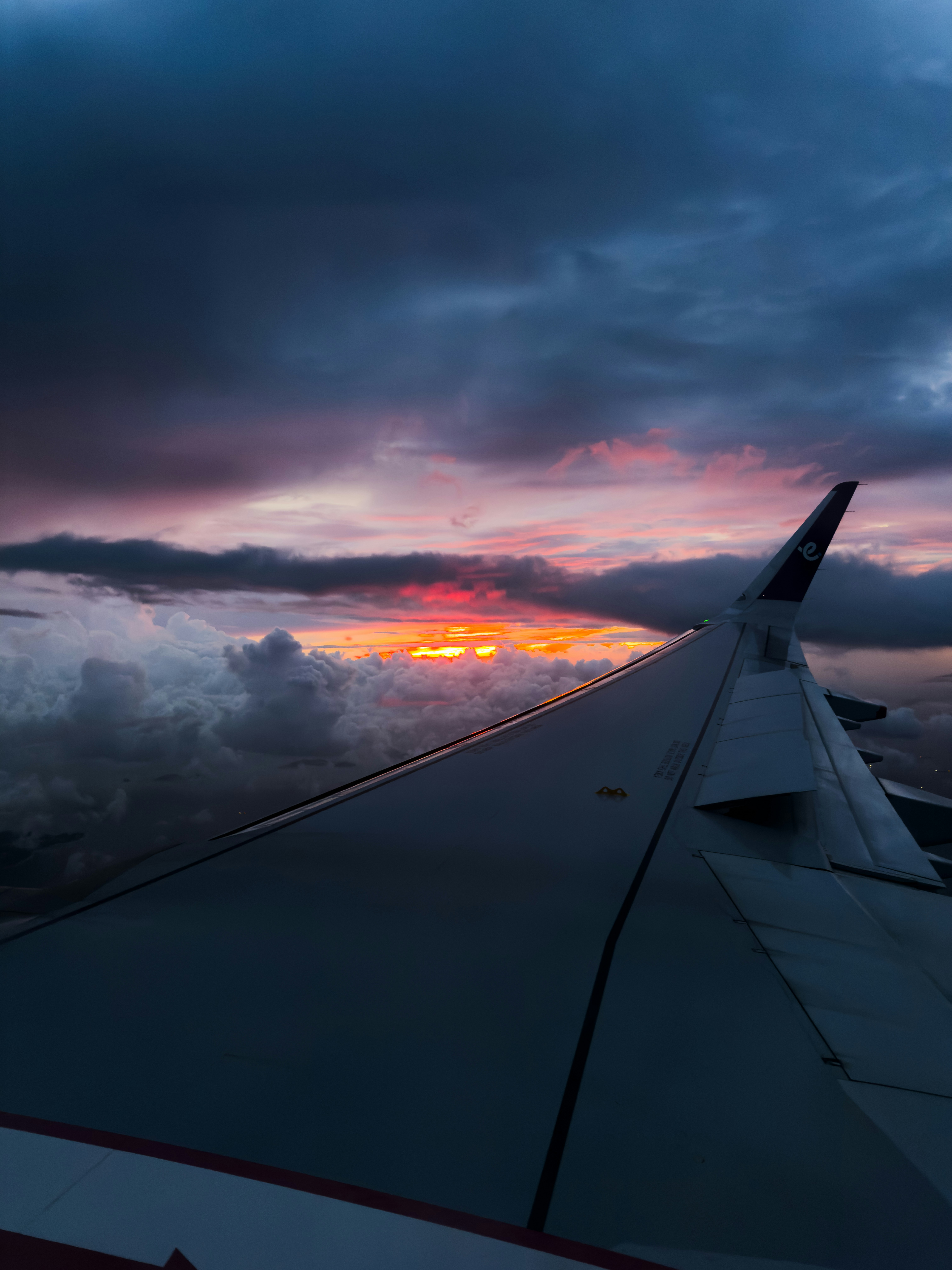Sunset seen from an airplane wing with dramatic clouds and a glowing horizon.