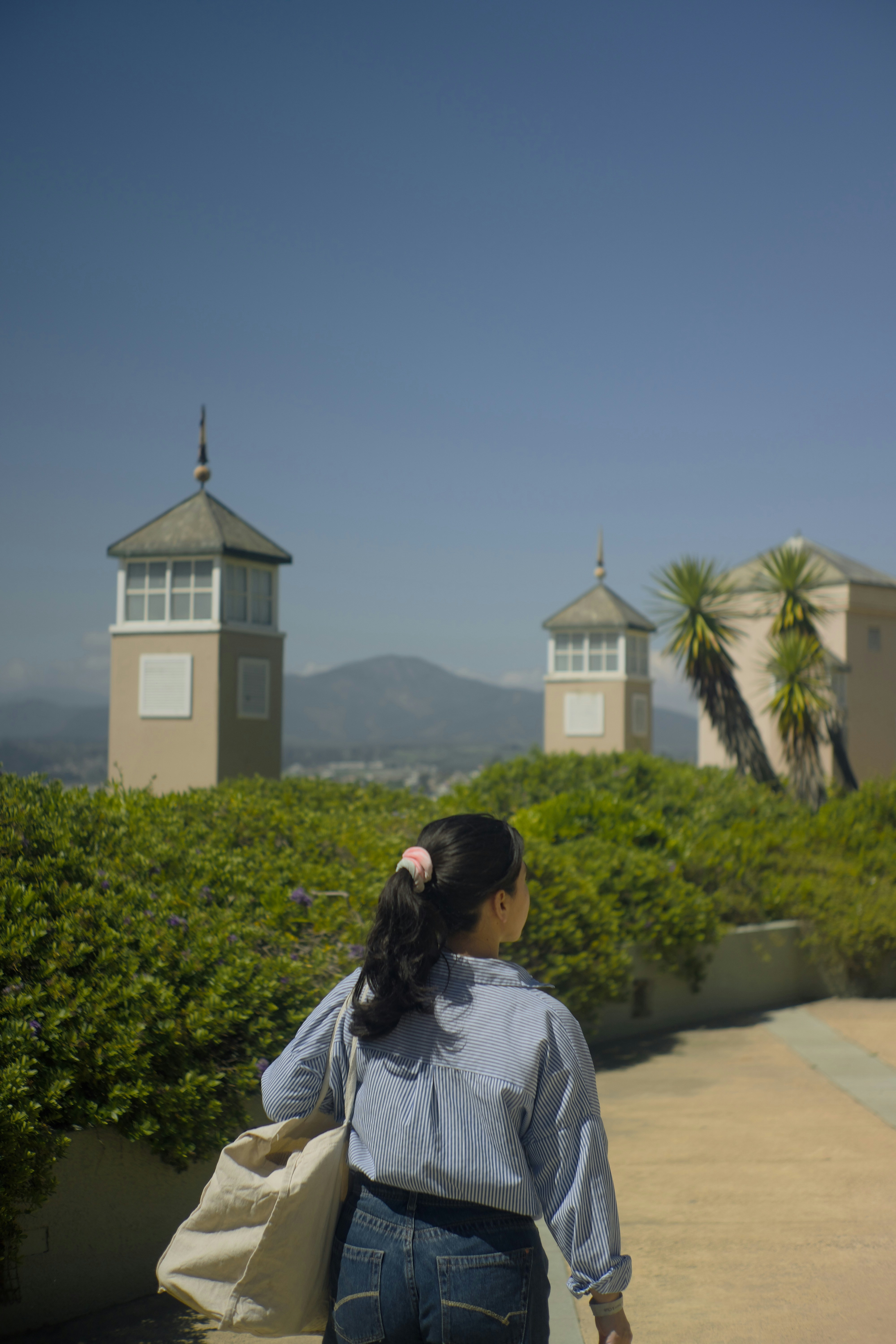 Girl in striped shirt walks toward rooftop towers under a clear blue sky
