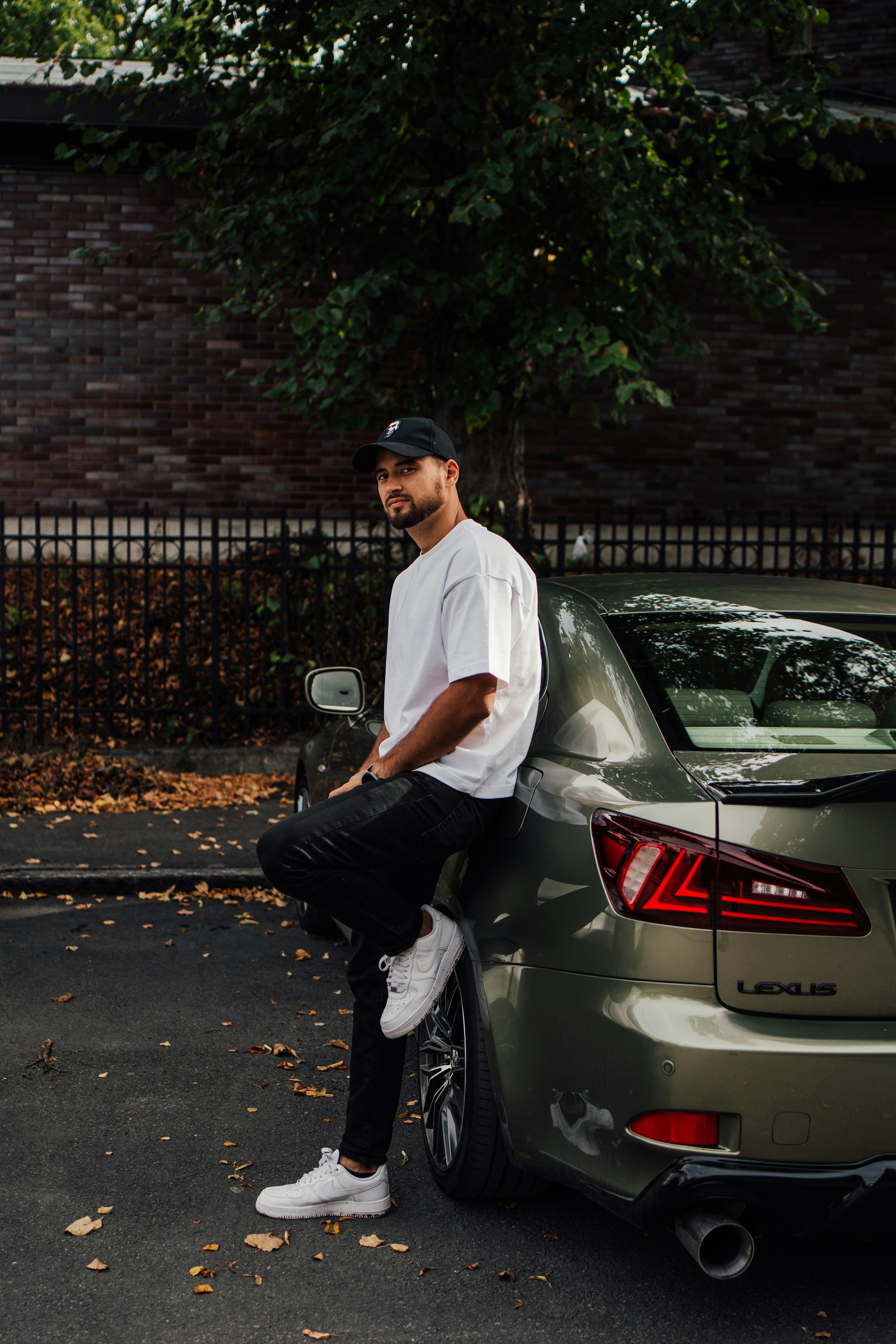 Man leaning on a green Lexus coupe in a parking lot during autumn