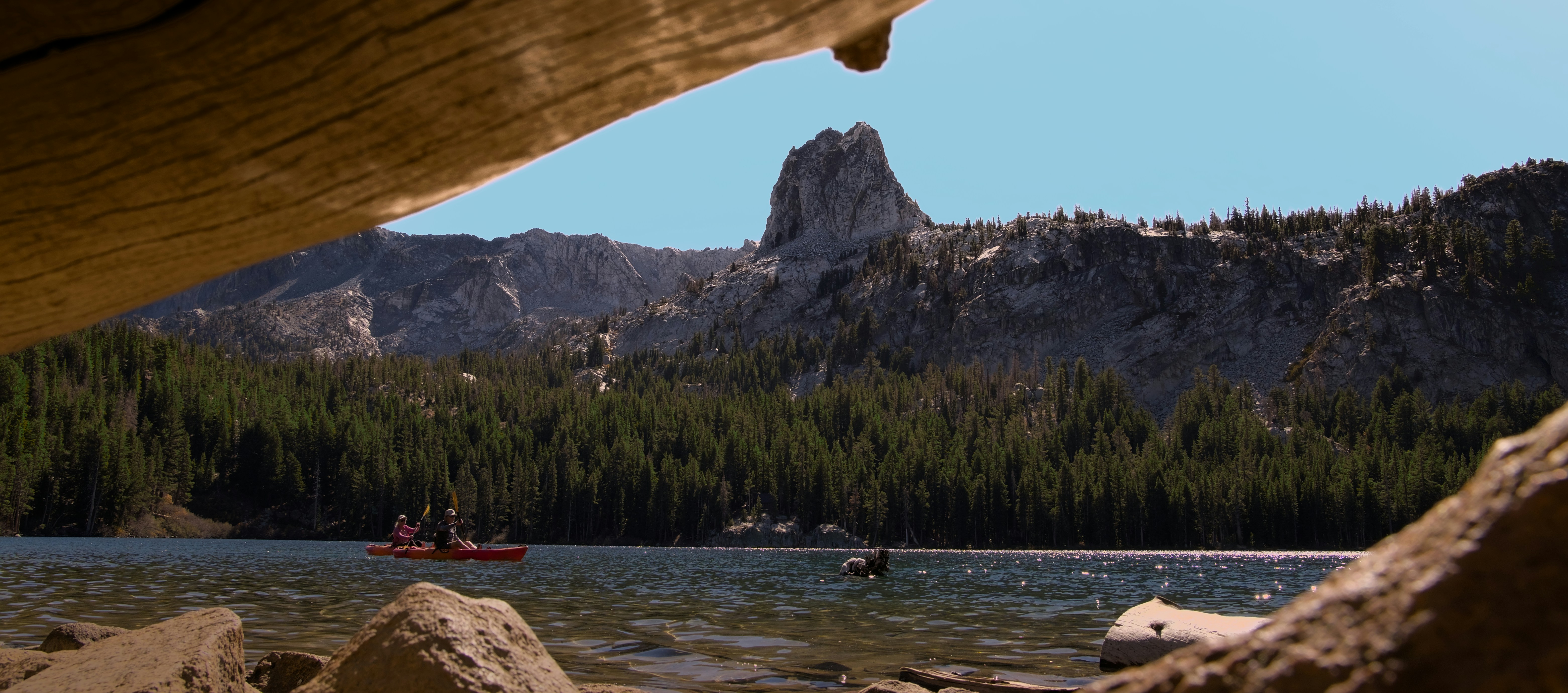 Two people in a red canoe on a mountain lake framed by foreground logs