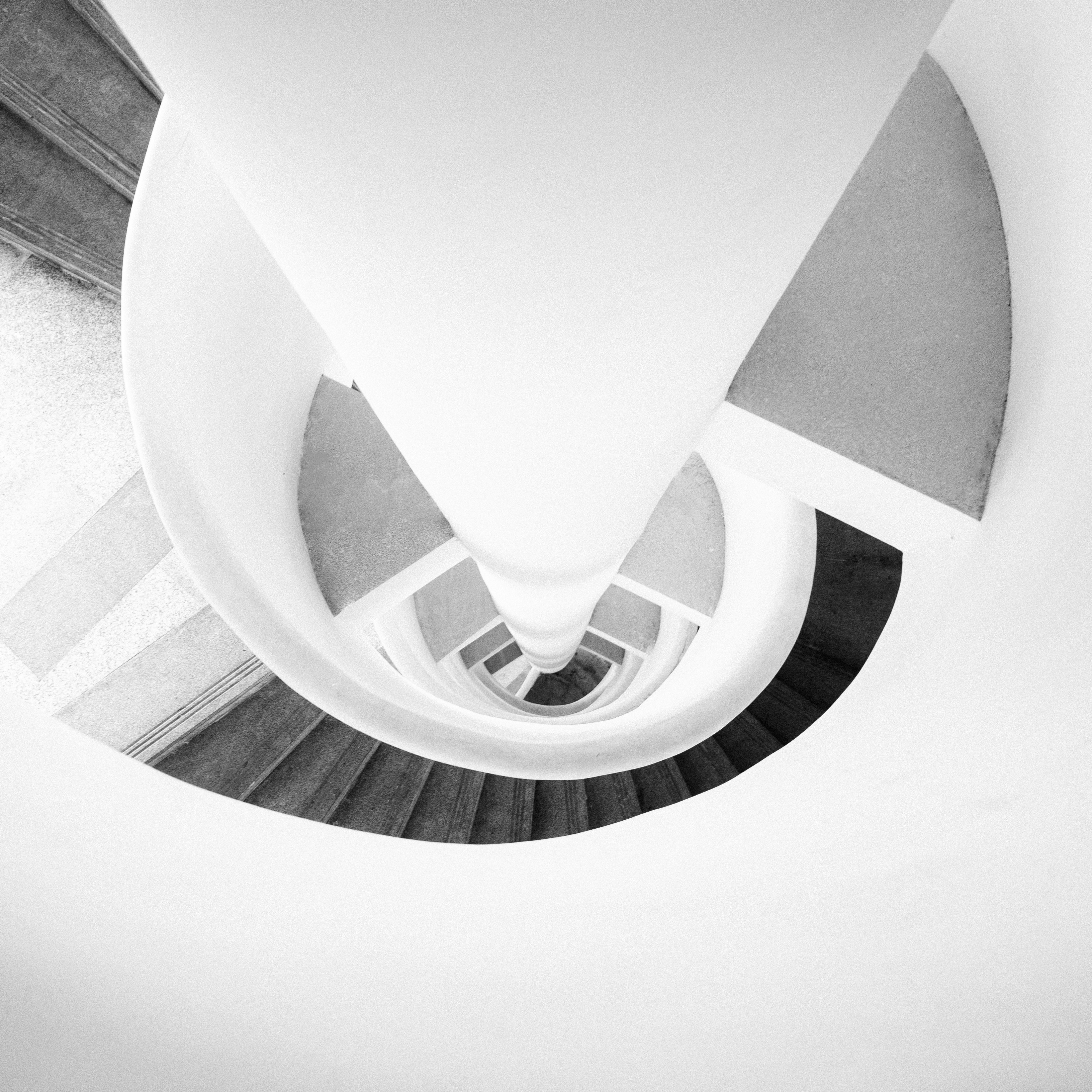 Monochrome spiral staircase viewed from above, leading into a vanishing point with strong circular geometry.