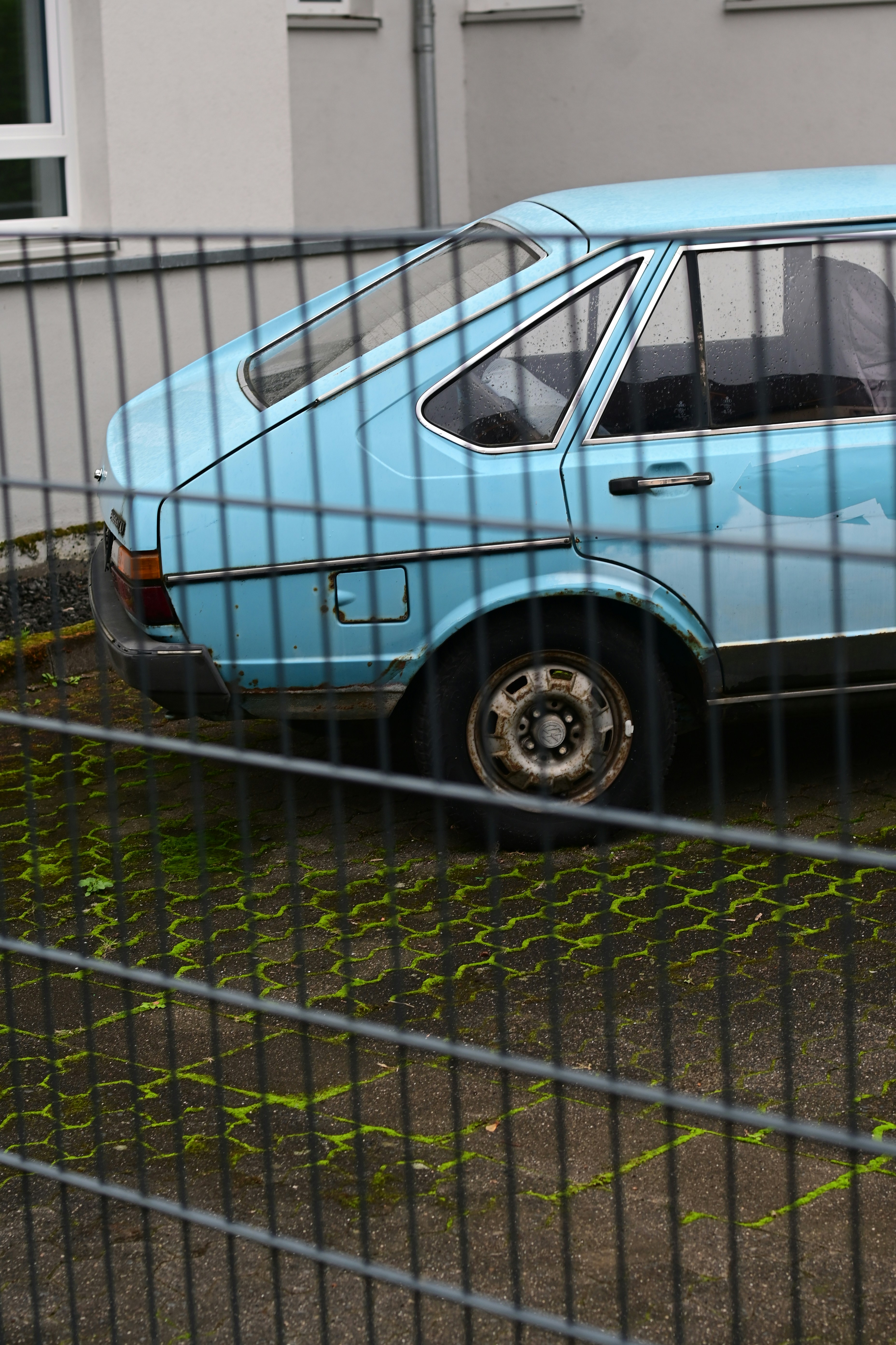 Blue Classic in Quiet Grit: A Car Behind Wrought Iron