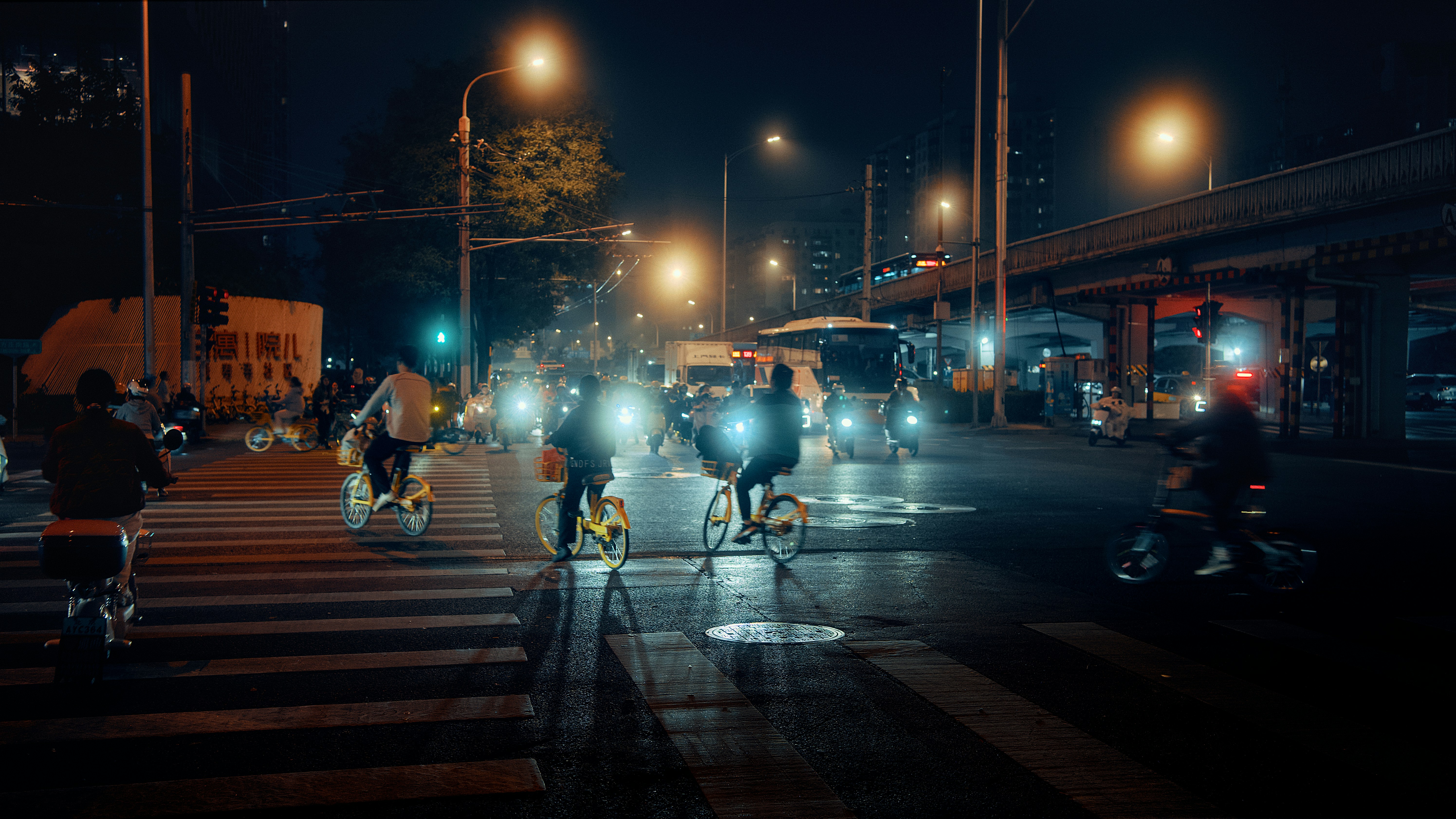 People riding bicycles across a city intersection at night under bright streetlights