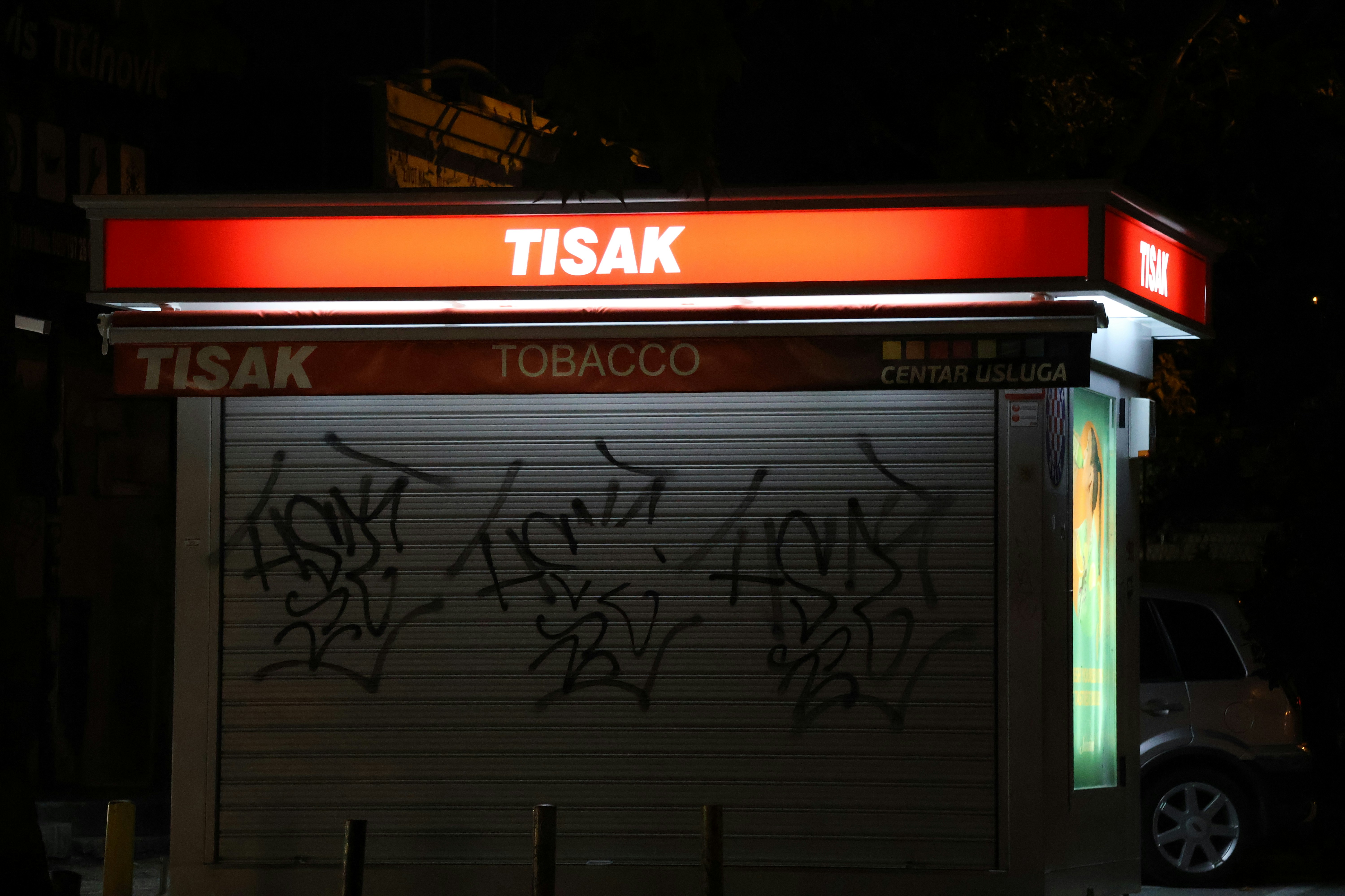 Neon Sign Over a Graffitied Tobacco Kiosk at Night