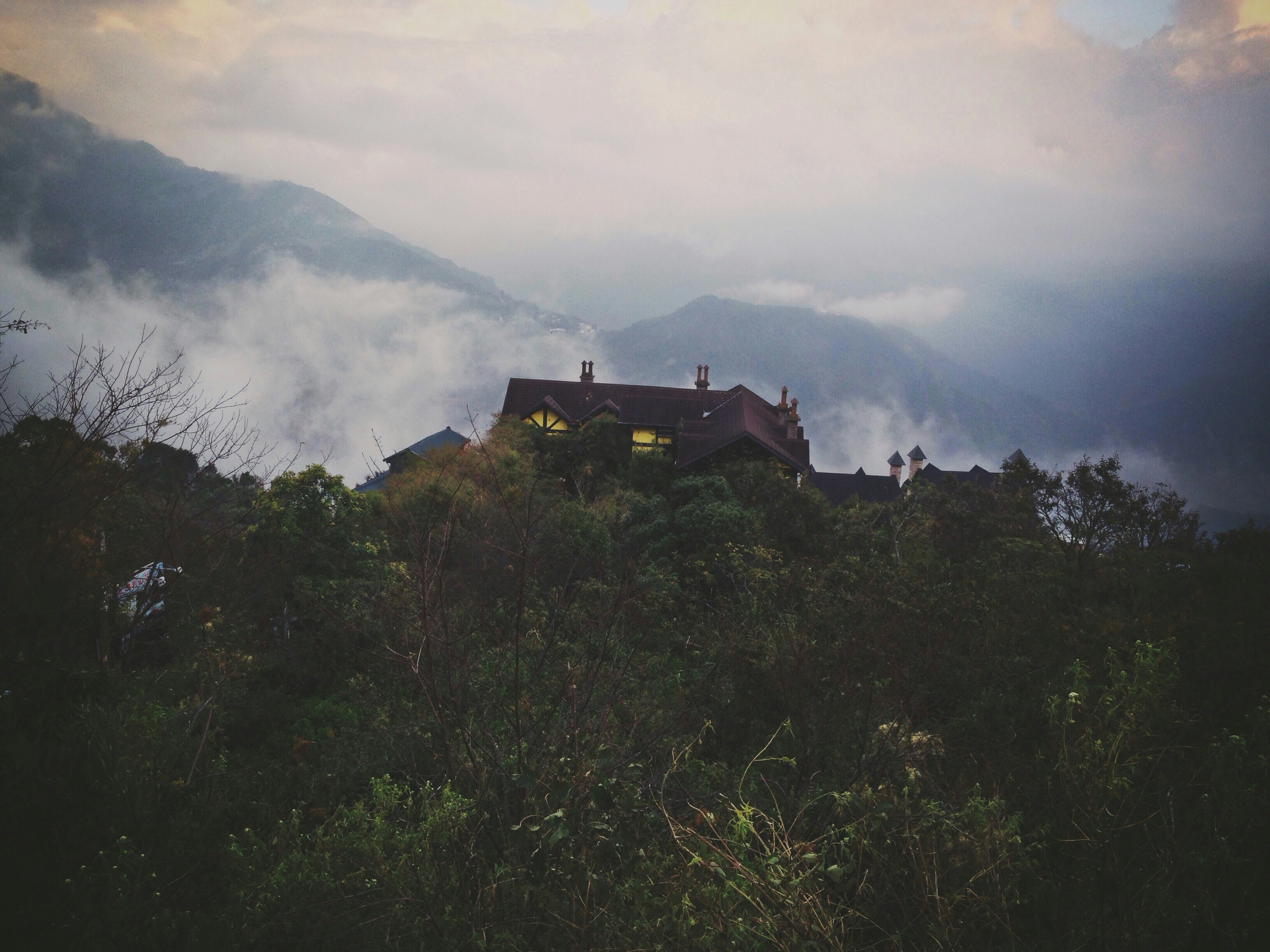 Silhouetted house nestled in lush greenery with mist-covered mountains in the background.